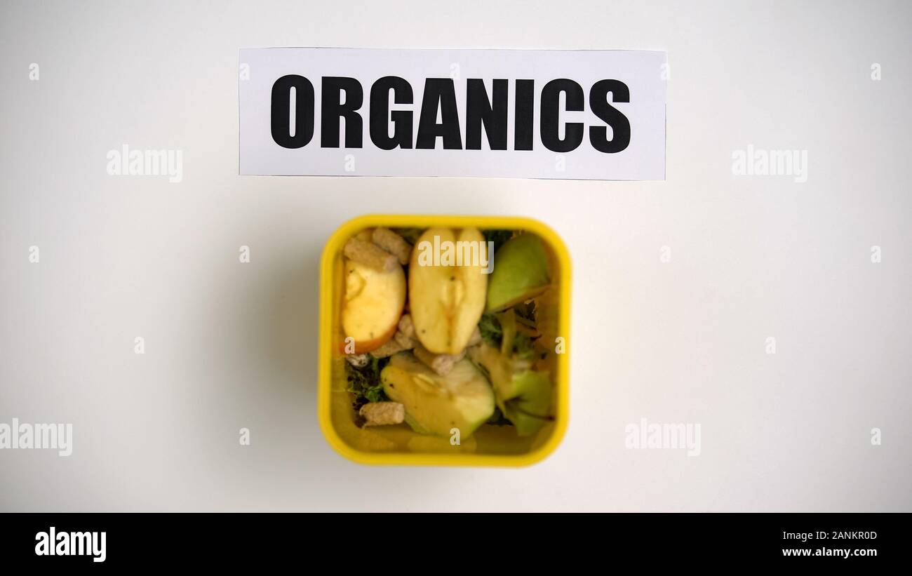 Container with biodegradable food standing near Organics word, waste ...