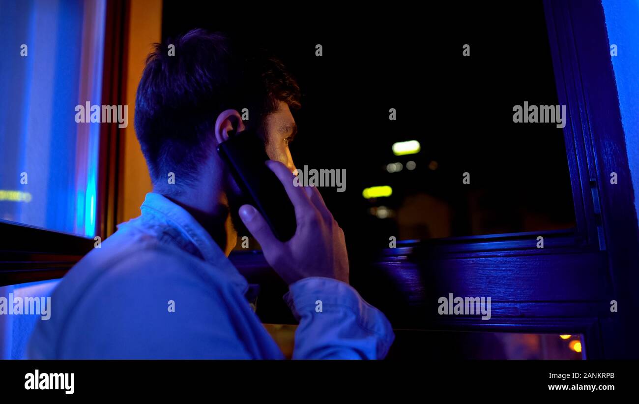 Sad man talking on phone and looking through window, waiting for wife ...