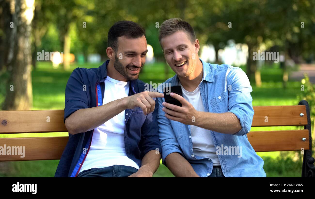 Best male friends watching photos on smartphone, having fun in park ...