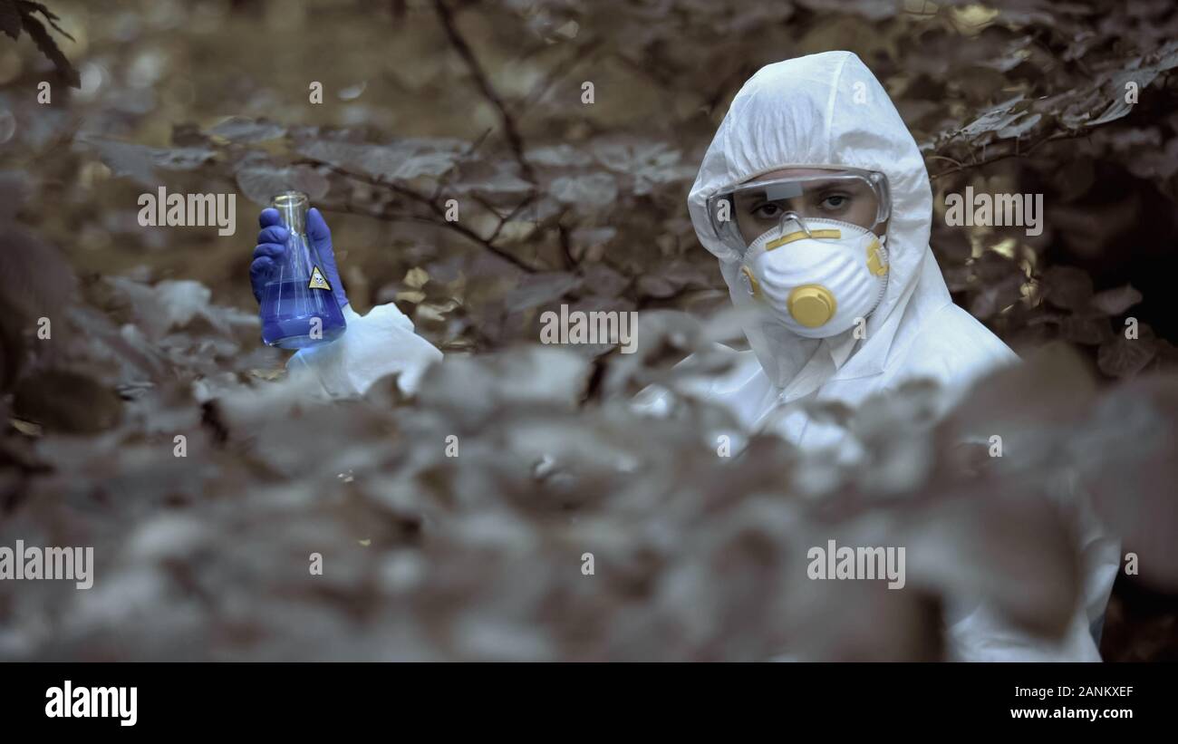 Female biologist in protective uniform holding infected water sample ...