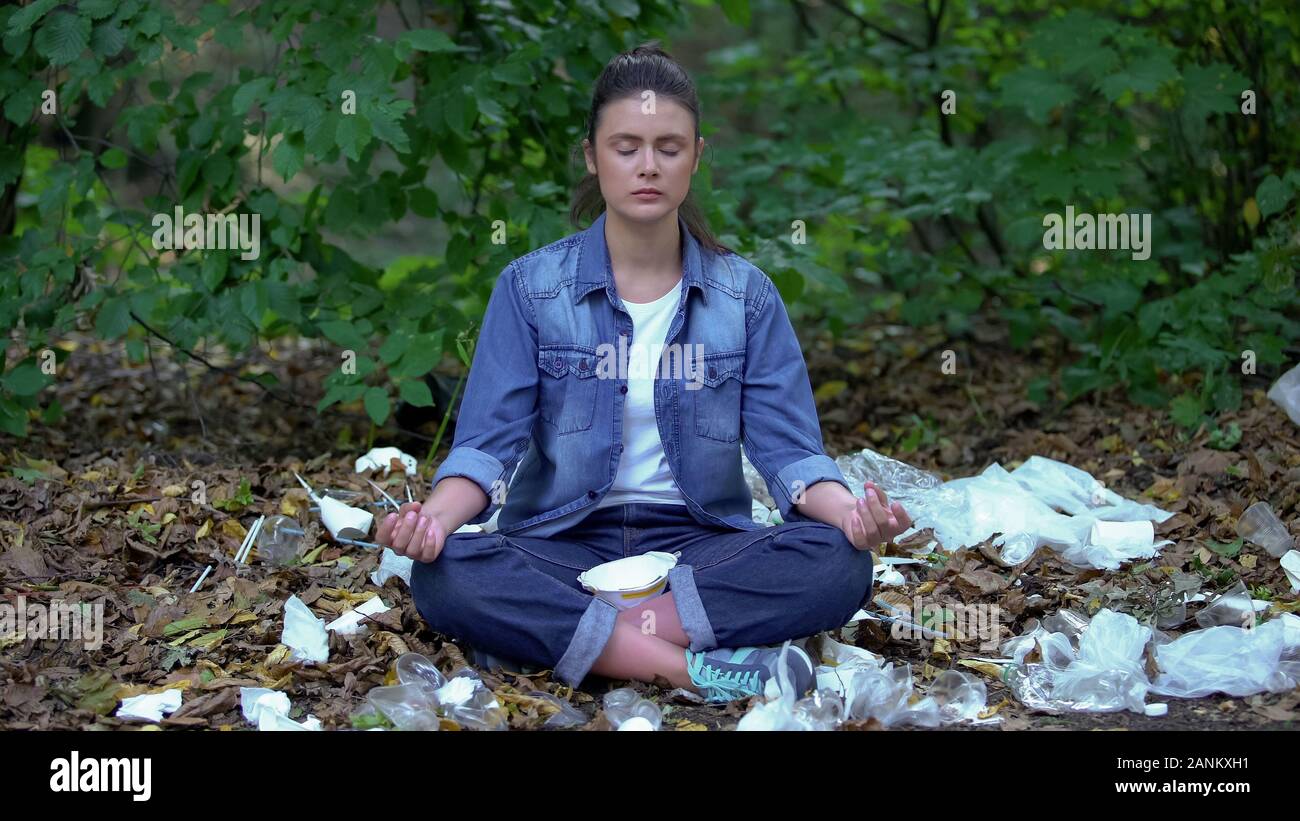 Woman meditating, sitting in lotus pose among plastic garbage ...