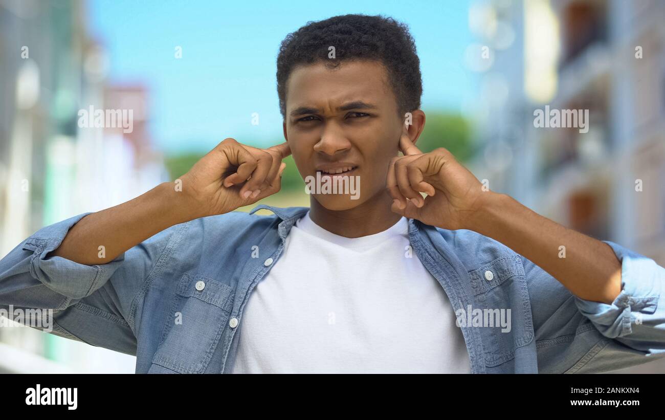 Afro-american teen guy suffering loud street noise, closing ears by ...