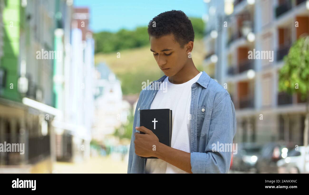Faithful mixed-race teen male looking at holy bible in hands, religion ...