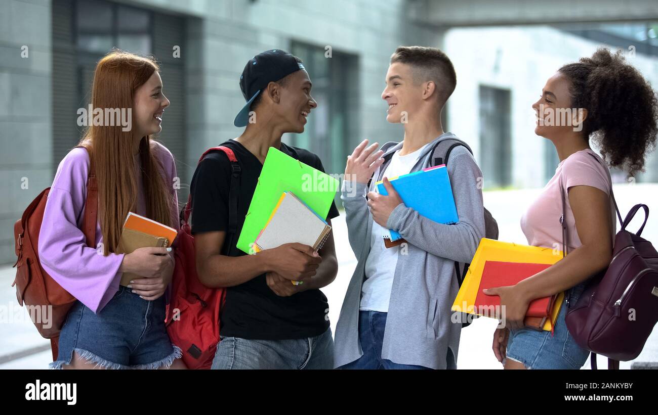 High school classmates with notebooks and backpacks talking campus ...