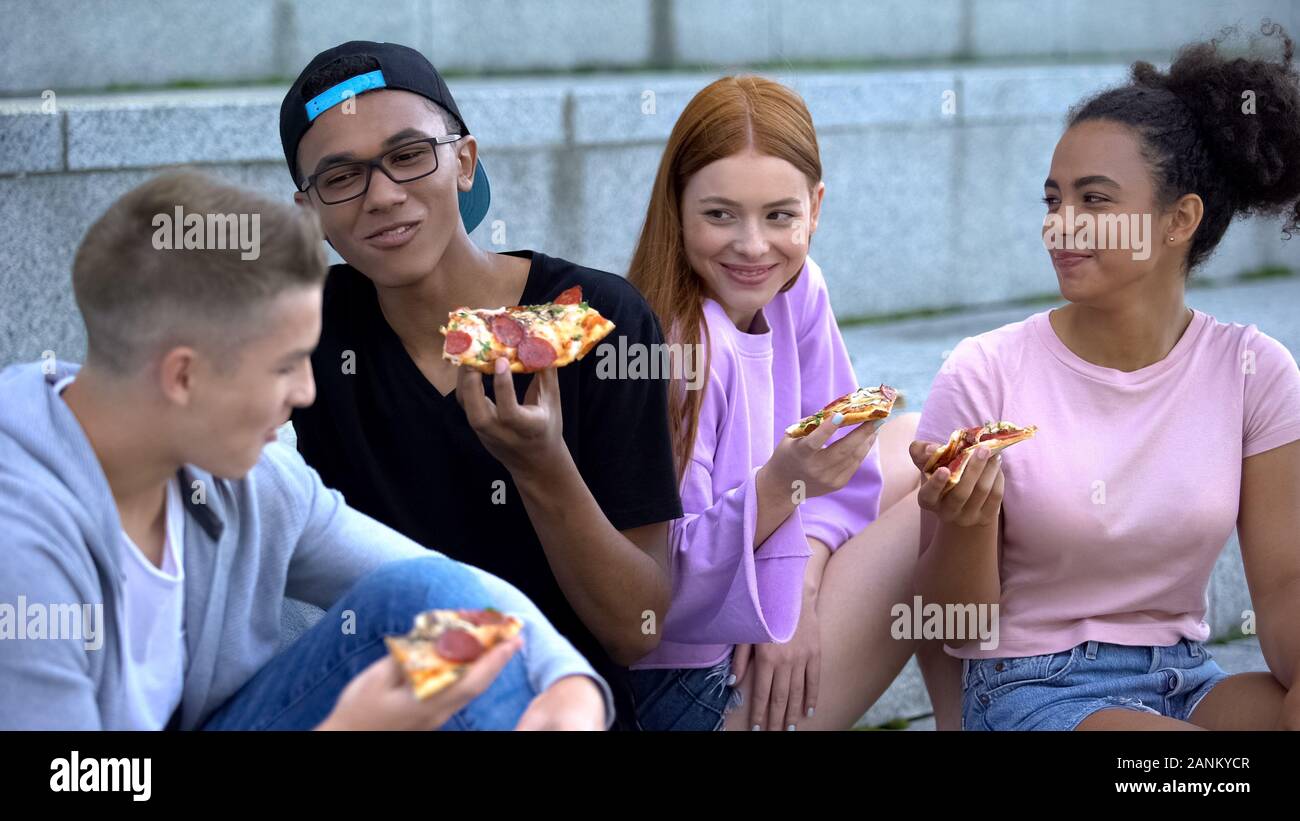 Joyful young people enjoying time together eating pizza outdoors ...