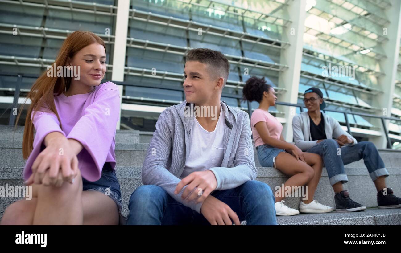 Young college students on outdoors date talking sitting campus stairs ...