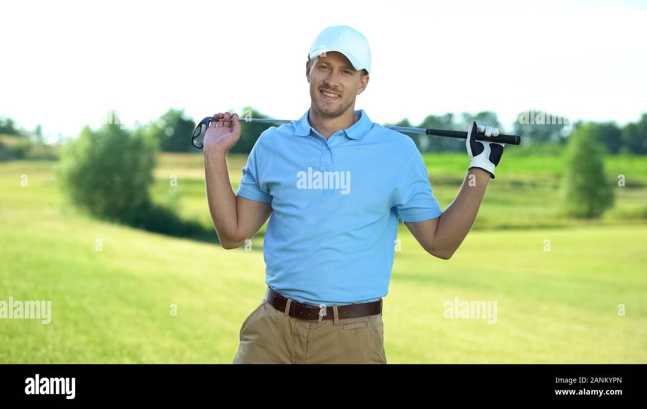 Confident golf player with club behind back smiling on camera at course ...
