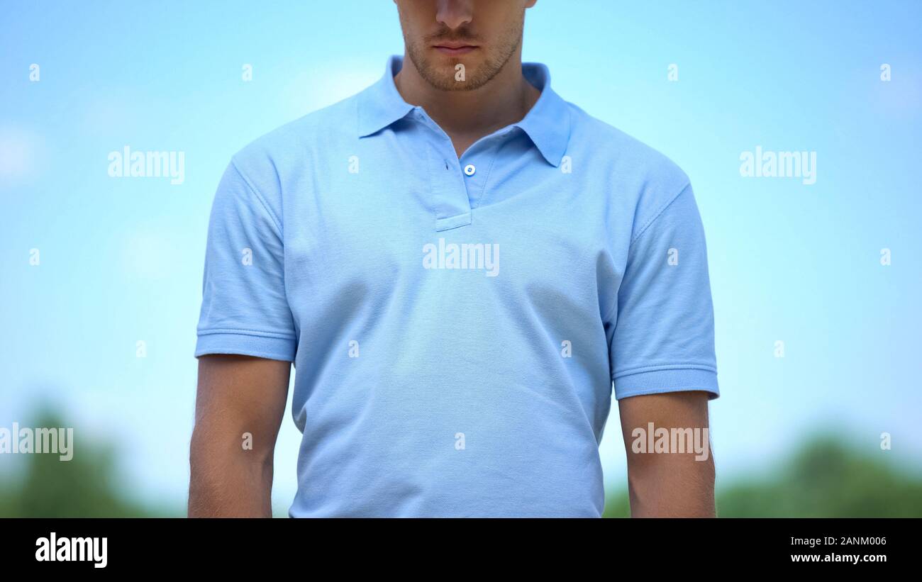 Depressed man in blue t-shirt sadly looking down outdoor, feeling ...