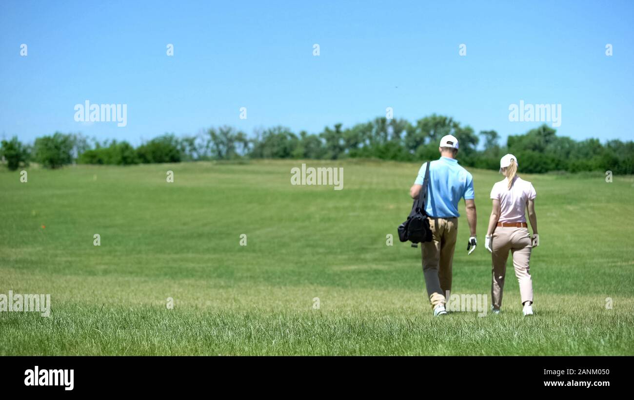 Couple of male and female golfers walking on course with clubs bag ...