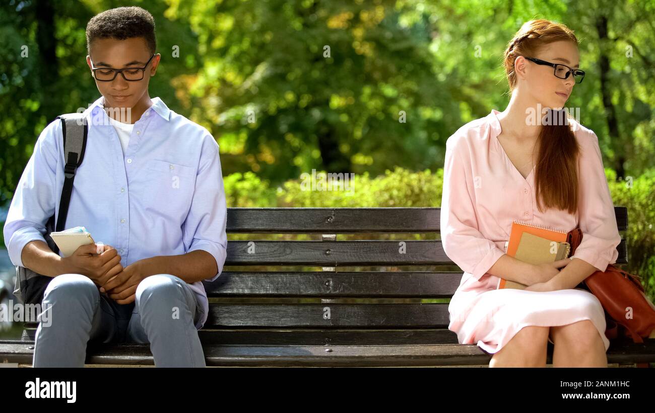 Shy teens sitting on different parts of bench, hesitating to tell about ...