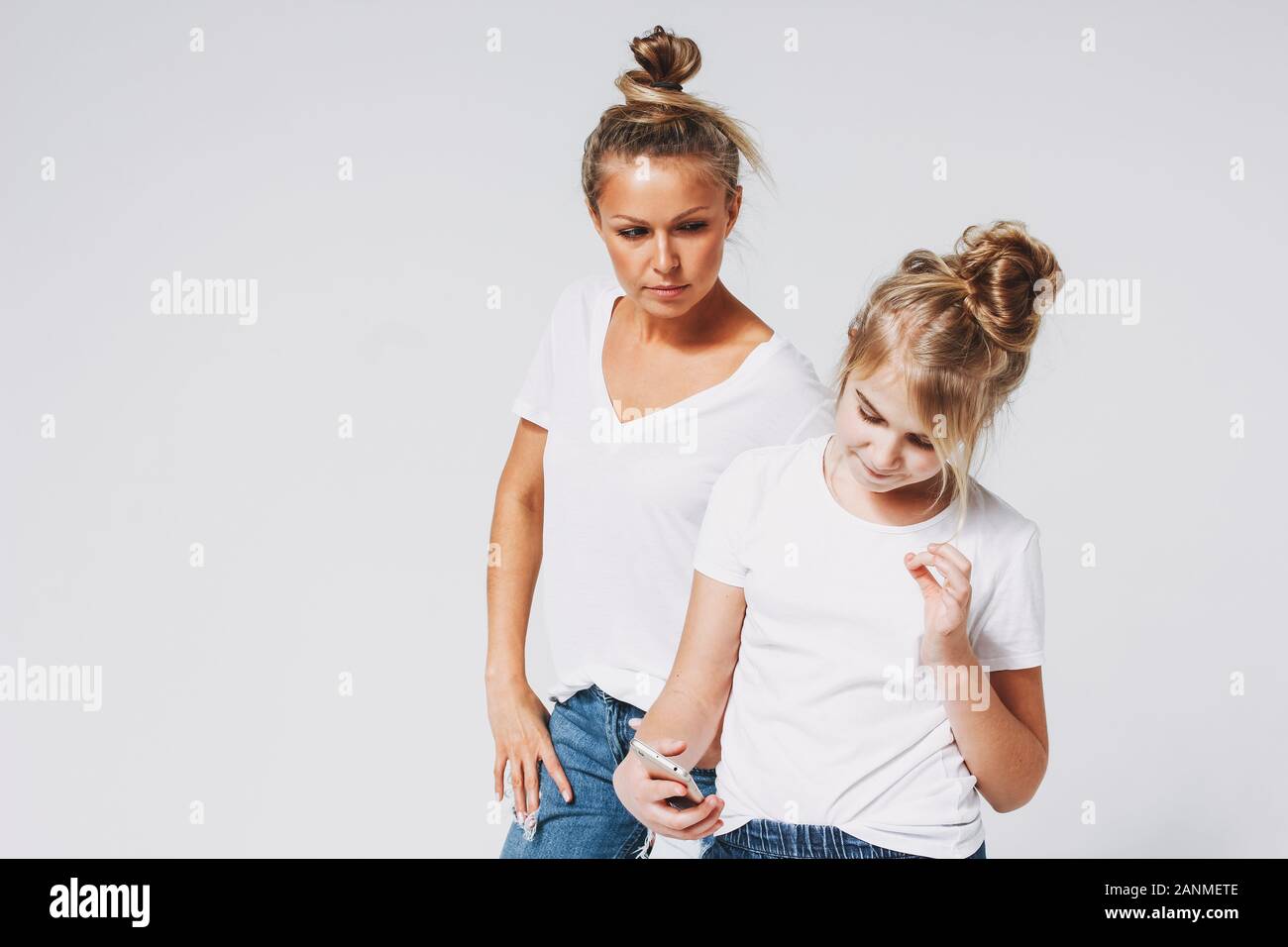Blonde suspicious mom and daughter in white t-shirts and jeans using ...