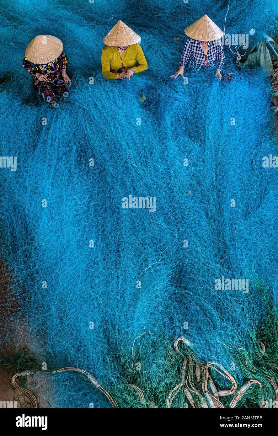 Vietnamese women in a fishing village weave and repair blue fishing ...