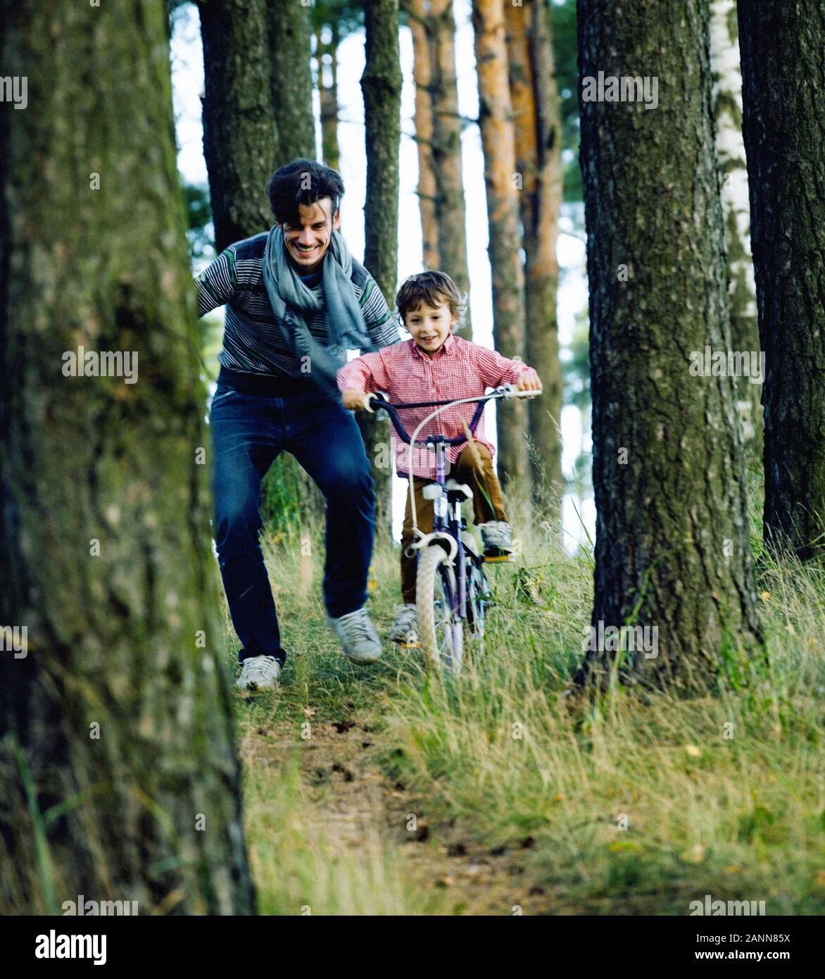 father learning his son to ride on bicycle outside, real happy family ...