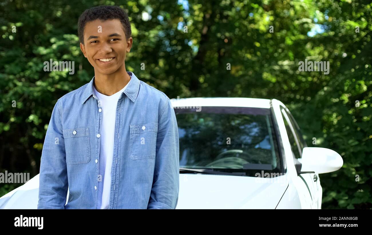 Young black male smiling on cam, leaning new automobile, driving ...