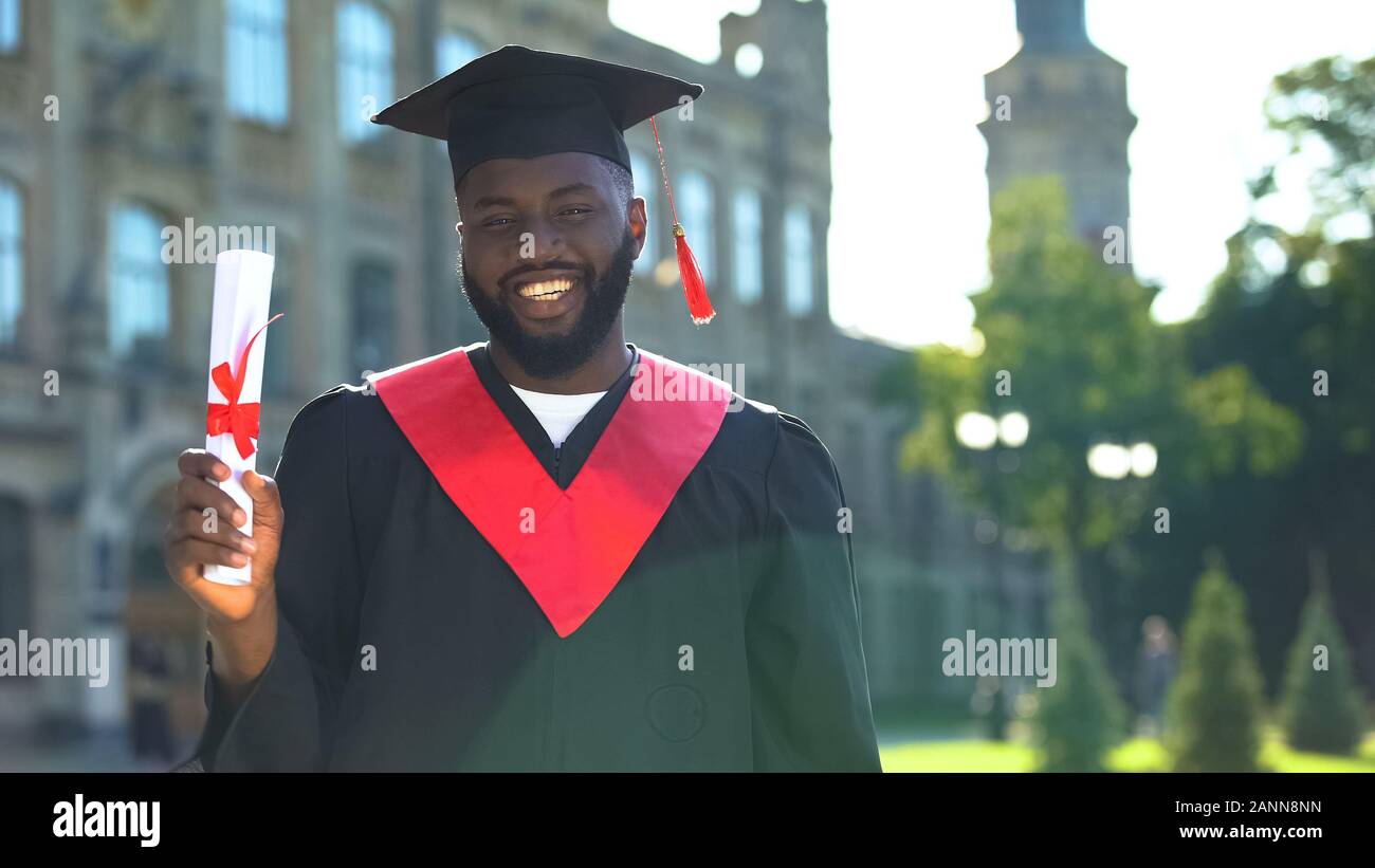 Excited afro-american student in graduation gown holding diploma ...