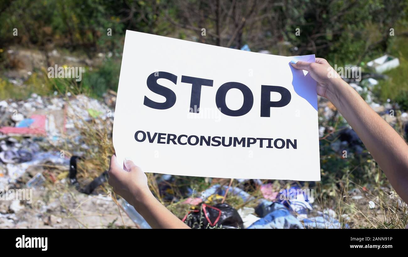 Stop overconsumption phrase on cardboard in hands against landfill ...