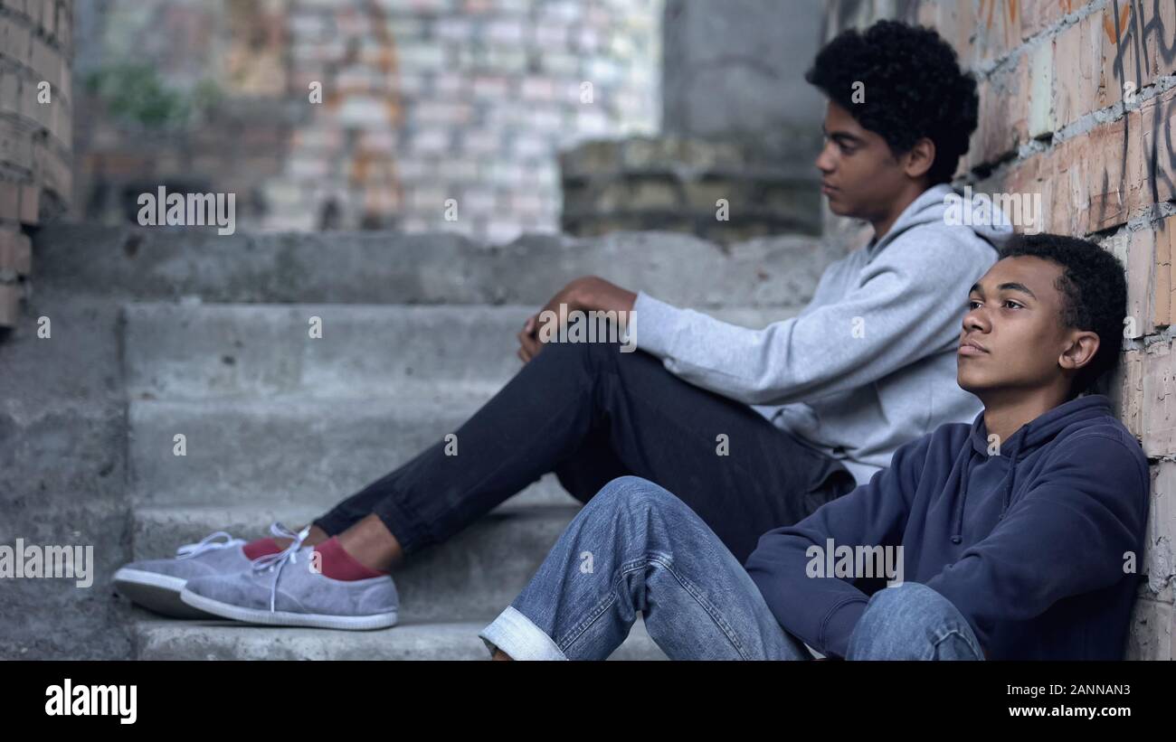 Poor lonely teenagers looking away sitting abandoned building ...
