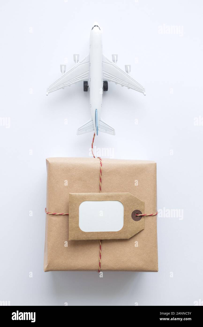 Flat lay of wrapped package with blank tag and airplane model on white ...