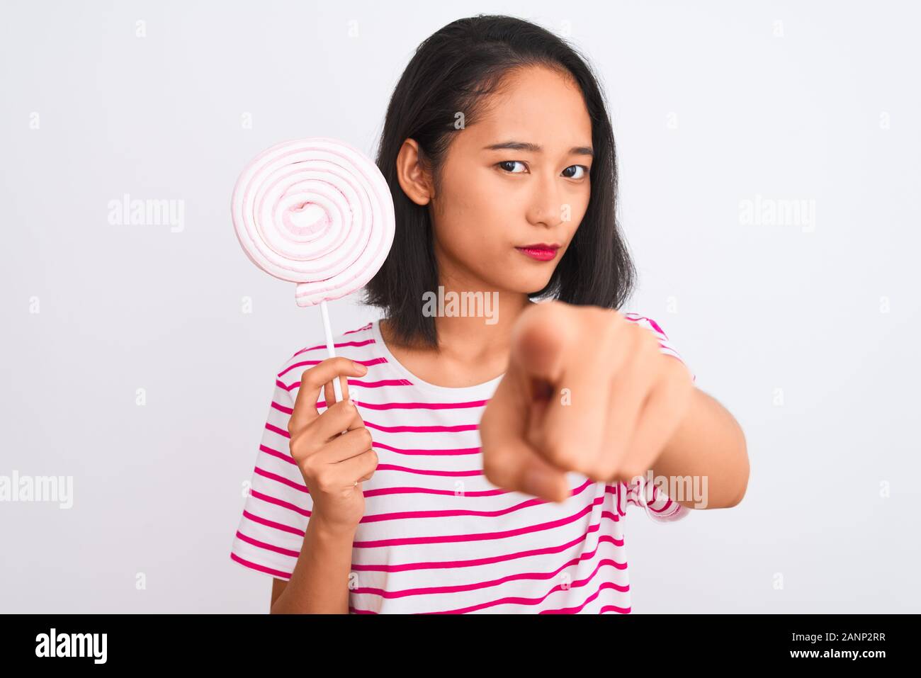 Young beautiful chinese woman eating lollipop standing over isolated ...