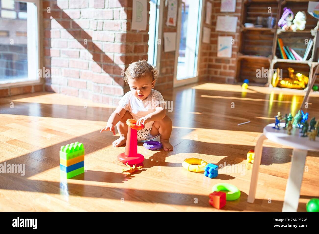 Adorable toddler building pyramid using hoops around lots of toys at ...