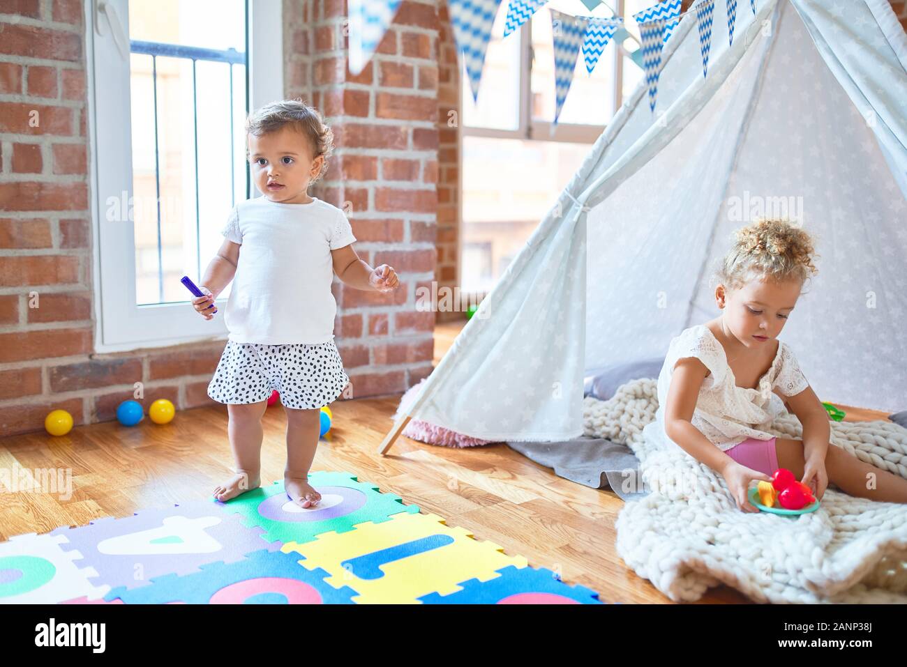 Beautiful toddlers playing inside tipi over blanket around lots of toys ...