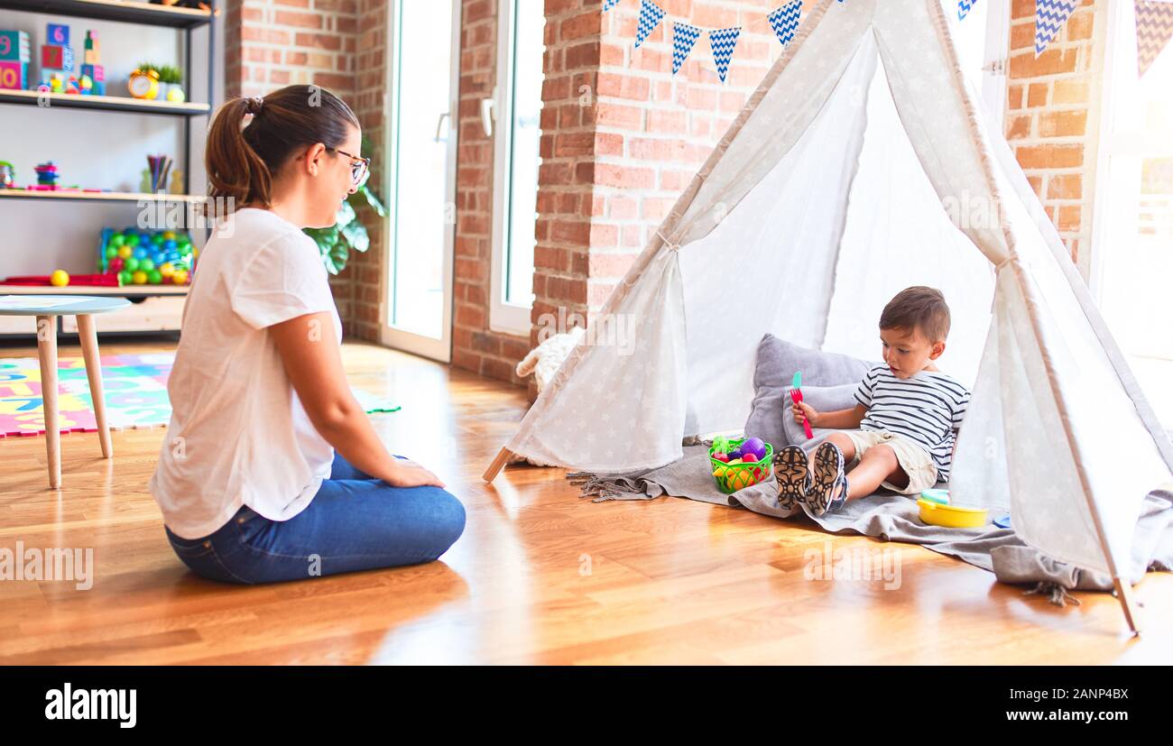 Beautiful teacher and toddler boy sitting on the floor playing inside ...
