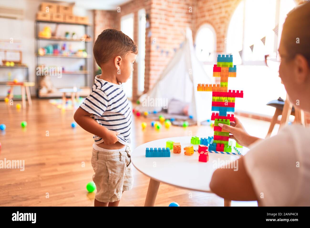 Beautiful teacher and toddler boy playing with construction blocks ...