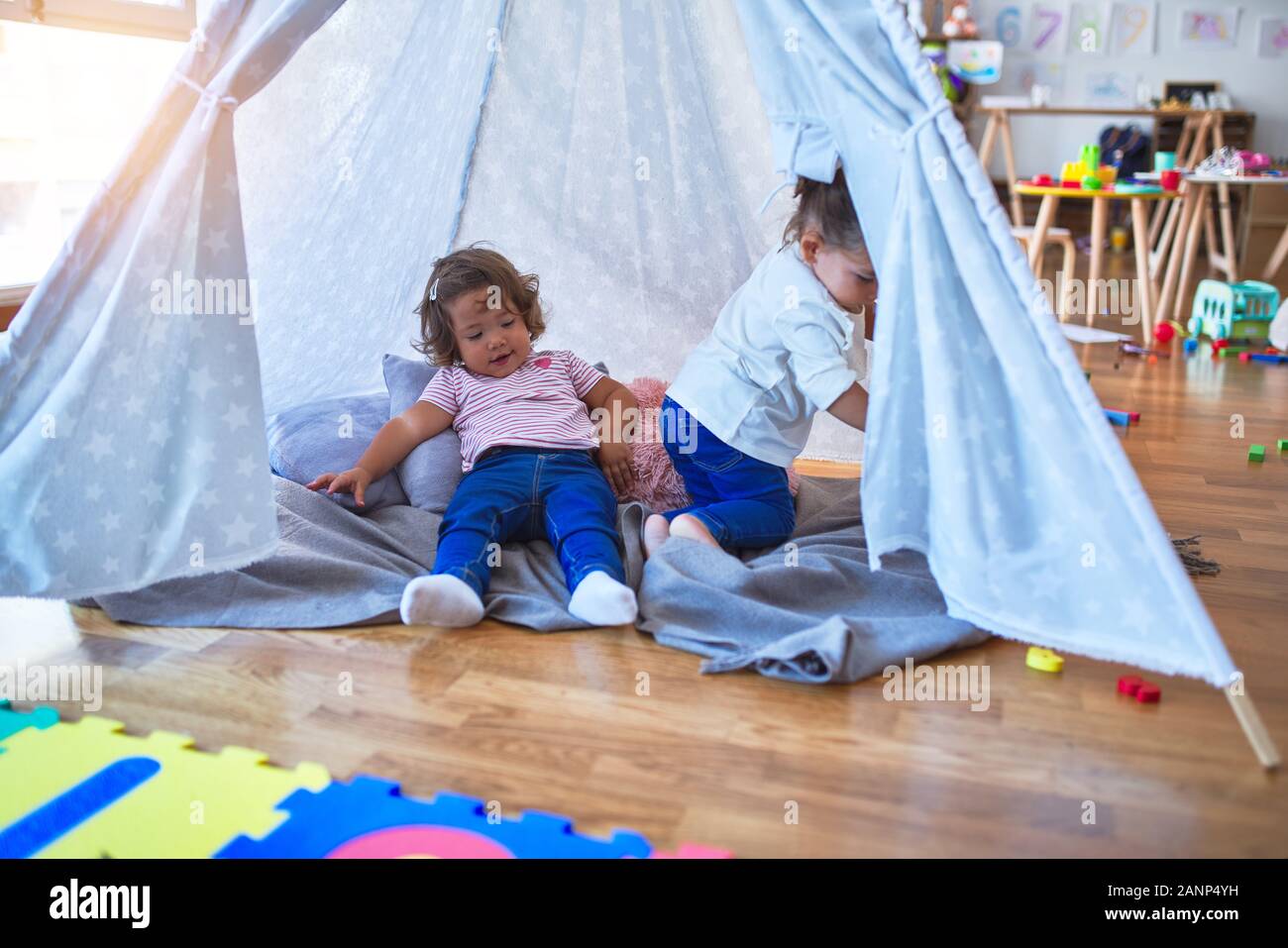 Adorable toddlers lying down over blanket inside tipi smiling at ...