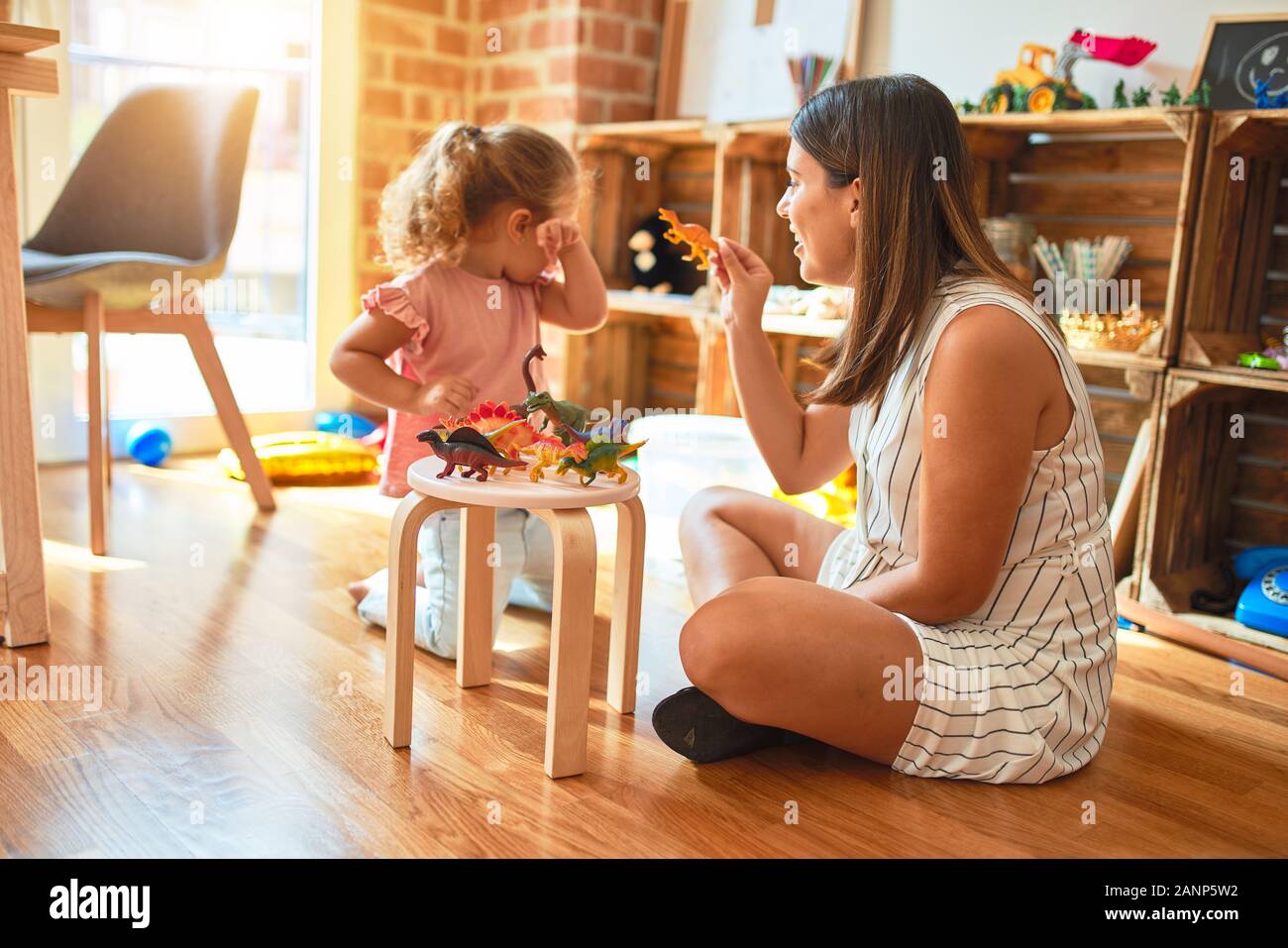 Beautiful teacher and blond student toddler girl playing with dinosaurs ...