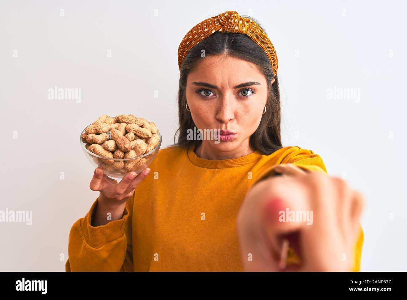 Young beautiful woman holding bowl with peanuts standing over isolated ...