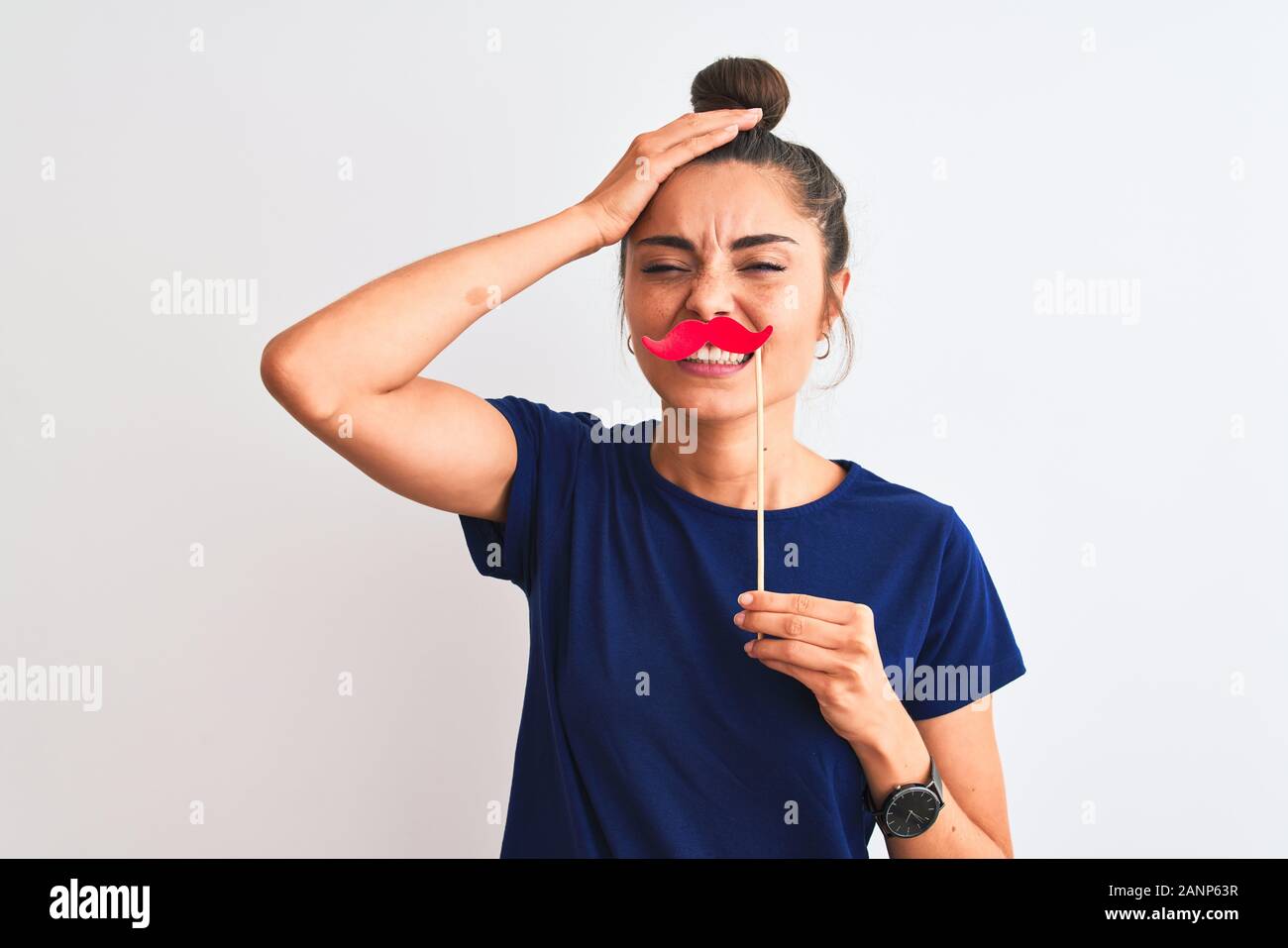 Young beautiful woman holding fanny party mustache over isolated white ...