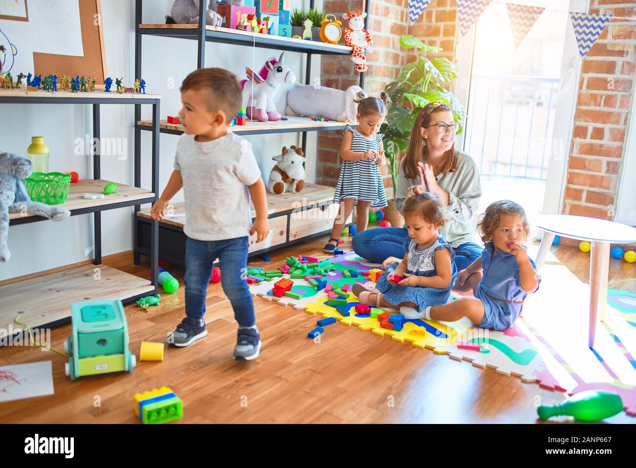 Beautiful teacher and group of toddlers playing around lots of toys at ...