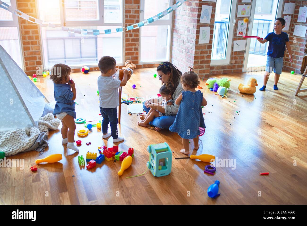 Beautiful teacher and group of toddlers playing around lots of toys at ...