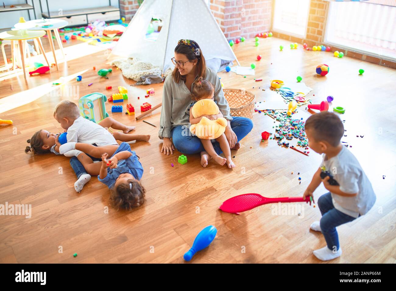 Beautiful teacher and group of toddlers playing around lots of toys at ...