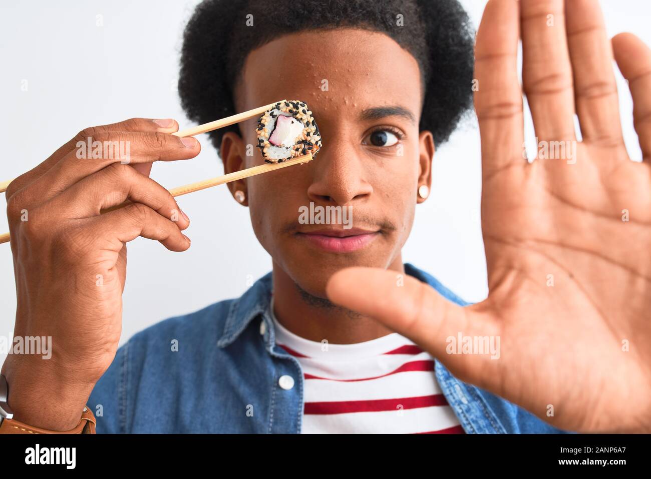 Young african american man eating sushi using chopsticks over isolated ...