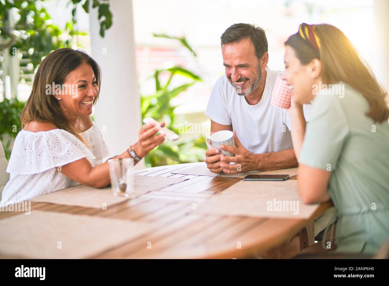 Beautiful family sitting on terrace drinking cup of coffee using ...