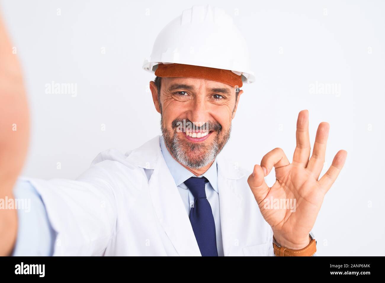 Middle age engineer man wearing helmet make selfie over isolated white ...