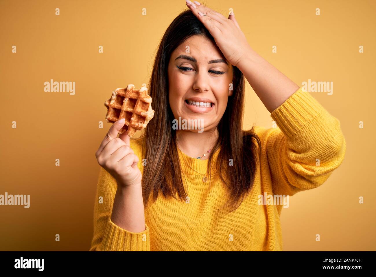 Young beautiful woman eating sweet waffle pastry over yellow background ...