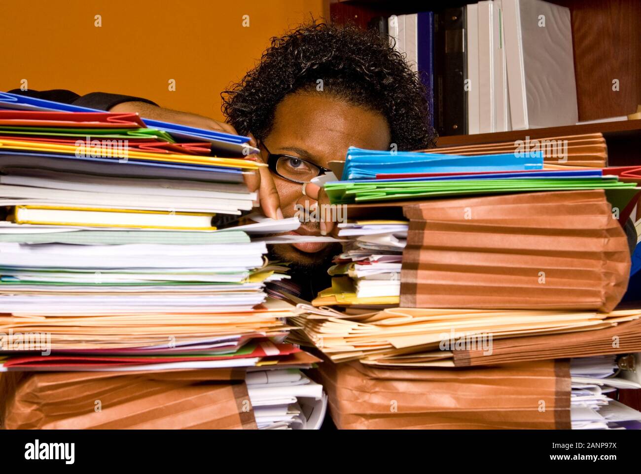 Over worked young man looking through a pile of colorful folders on his ...