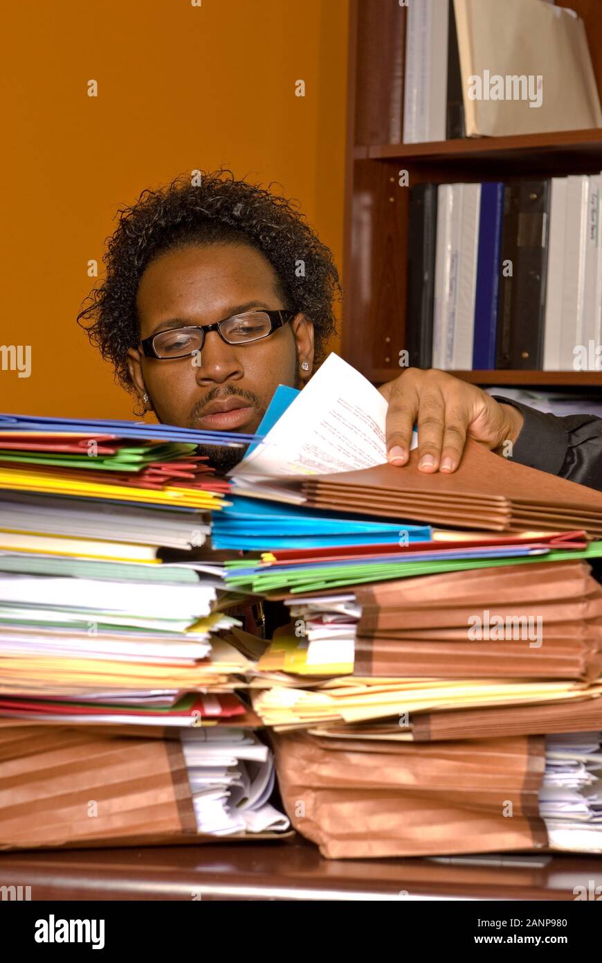 Over worked young man looking through a pile of colorful folders on his ...