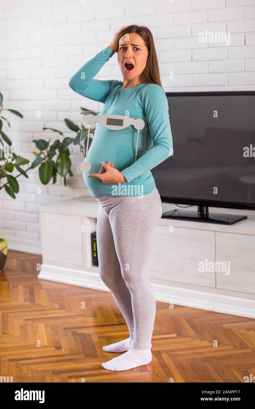 Pregnant woman is in shock because of her weight while she is holding ...