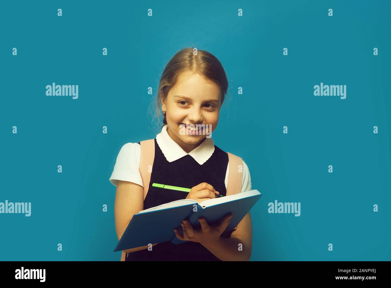 Pupil writes in blue book with green marker. Girl with braids and smile ...