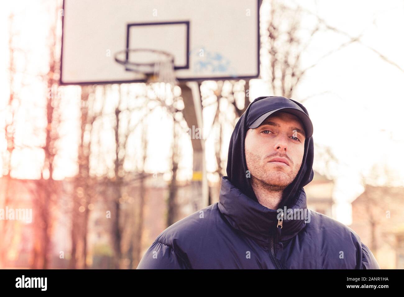 portrait of young rapper posing in the middle of an outdoor basketball ...