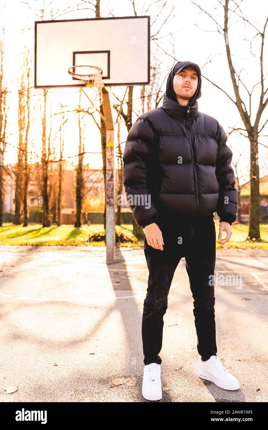 portrait of young rapper posing in the middle of an outdoor basketball ...