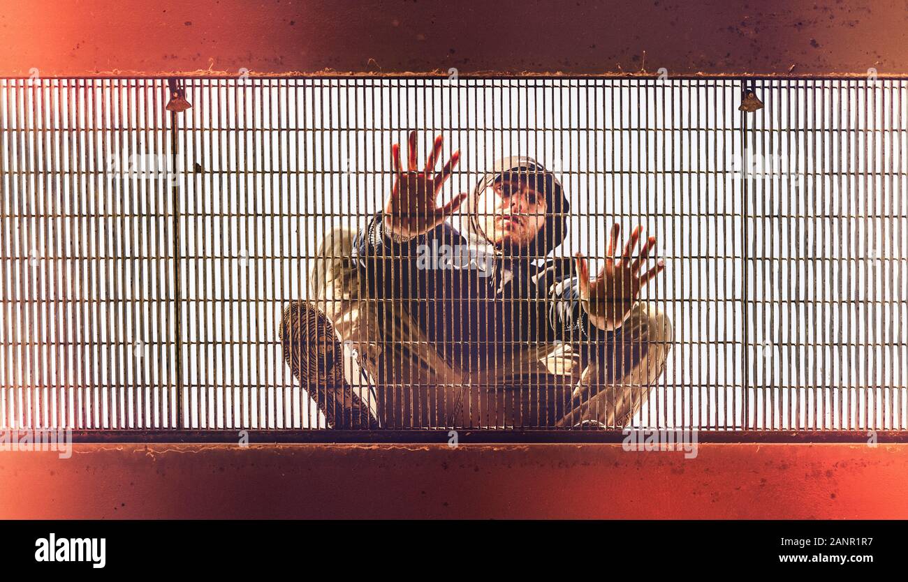 portrait of young rapper posing behind the metal grate of a bridge in ...