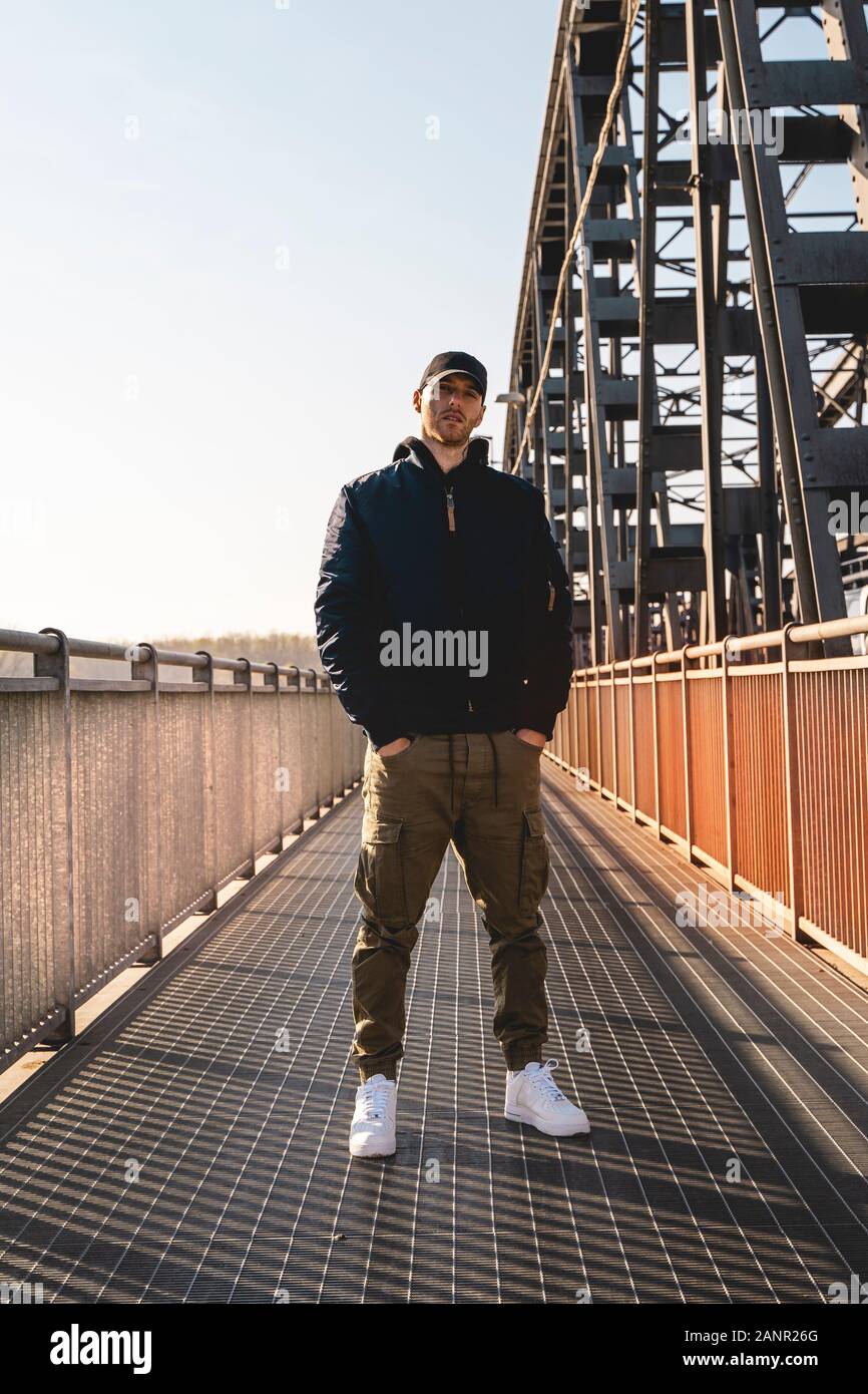 portrait of young rapper posing under a metal bridge in the suburbs ...