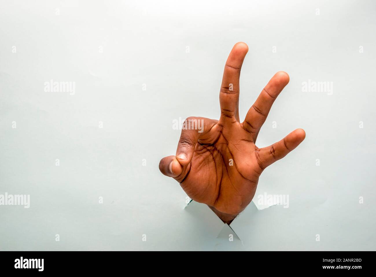black person hand through a hole in a cardboard making ok sign, showing ...