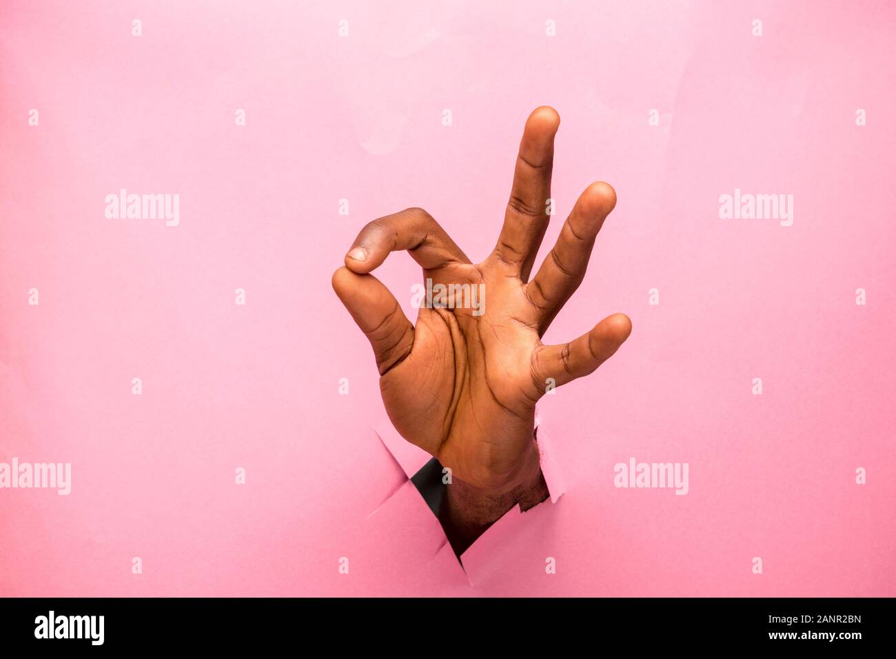 black person hand through a hole in a cardboard making ok sign, showing ...