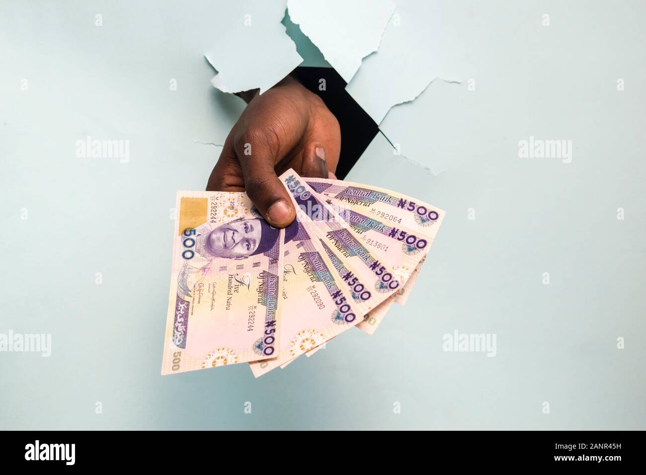 hand of a black person through a tear in a cardboard paper holding some ...
