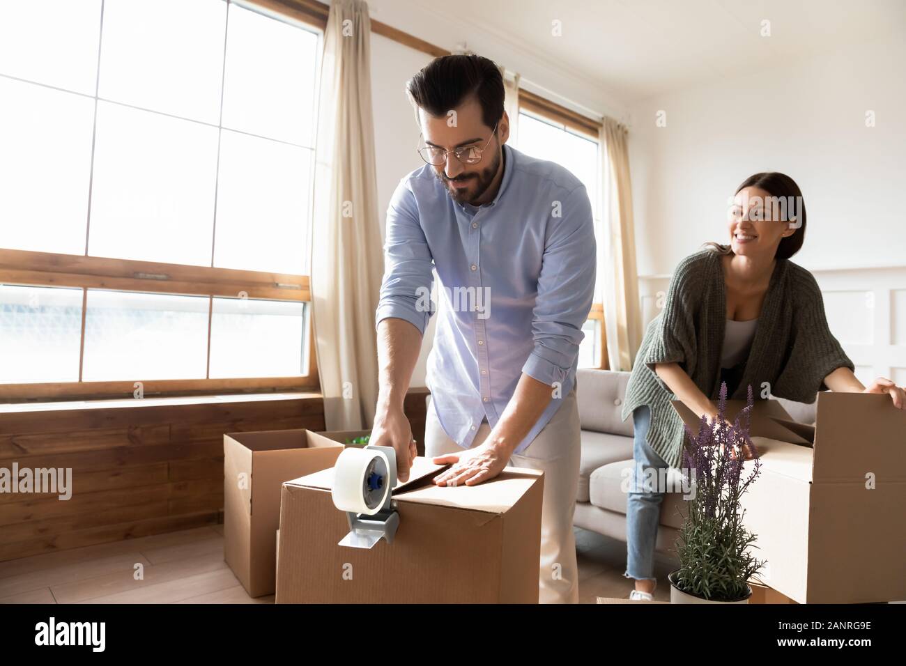 Happy young family packing boxes with tape dispenser Stock Photo - Alamy